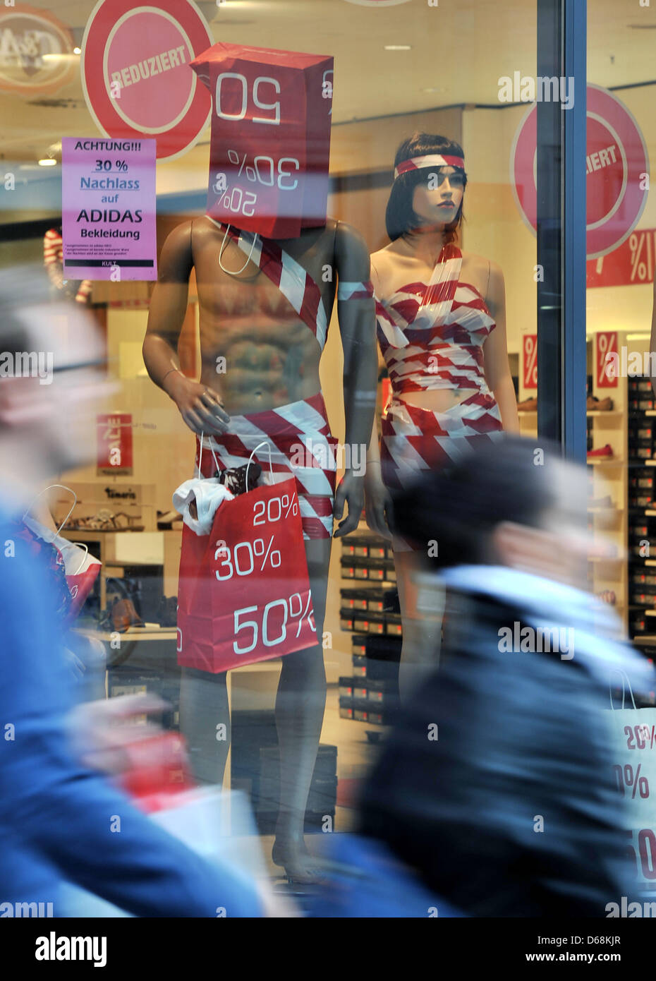 Pedestrians walk past a display window advertising reduced prices on ...