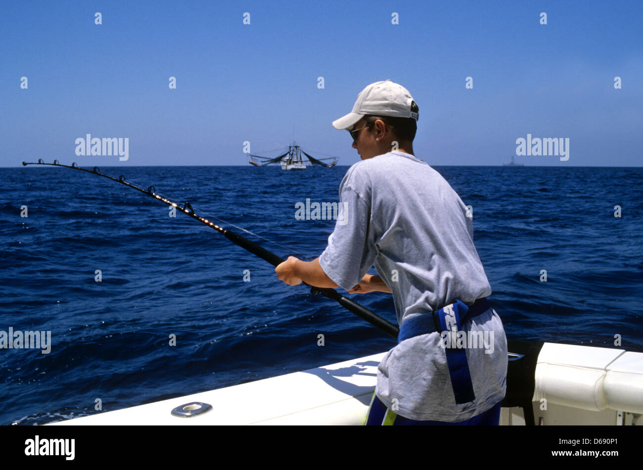 Young boy reeling in a king mackerel near a shrimp boat in the Gulf of ...