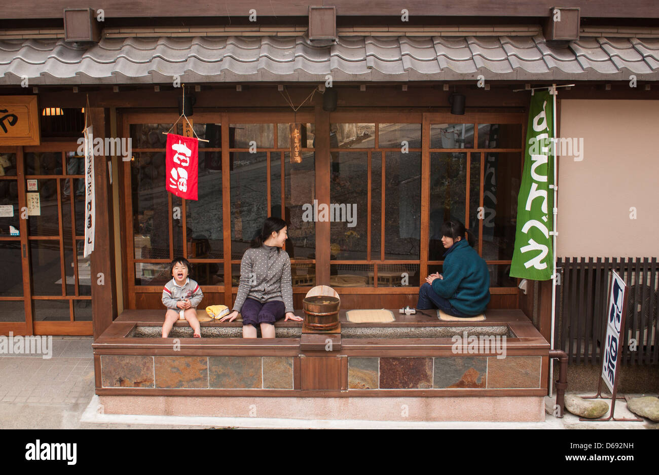 A mother and her son soak their feet in hot spring water outside a shop ...