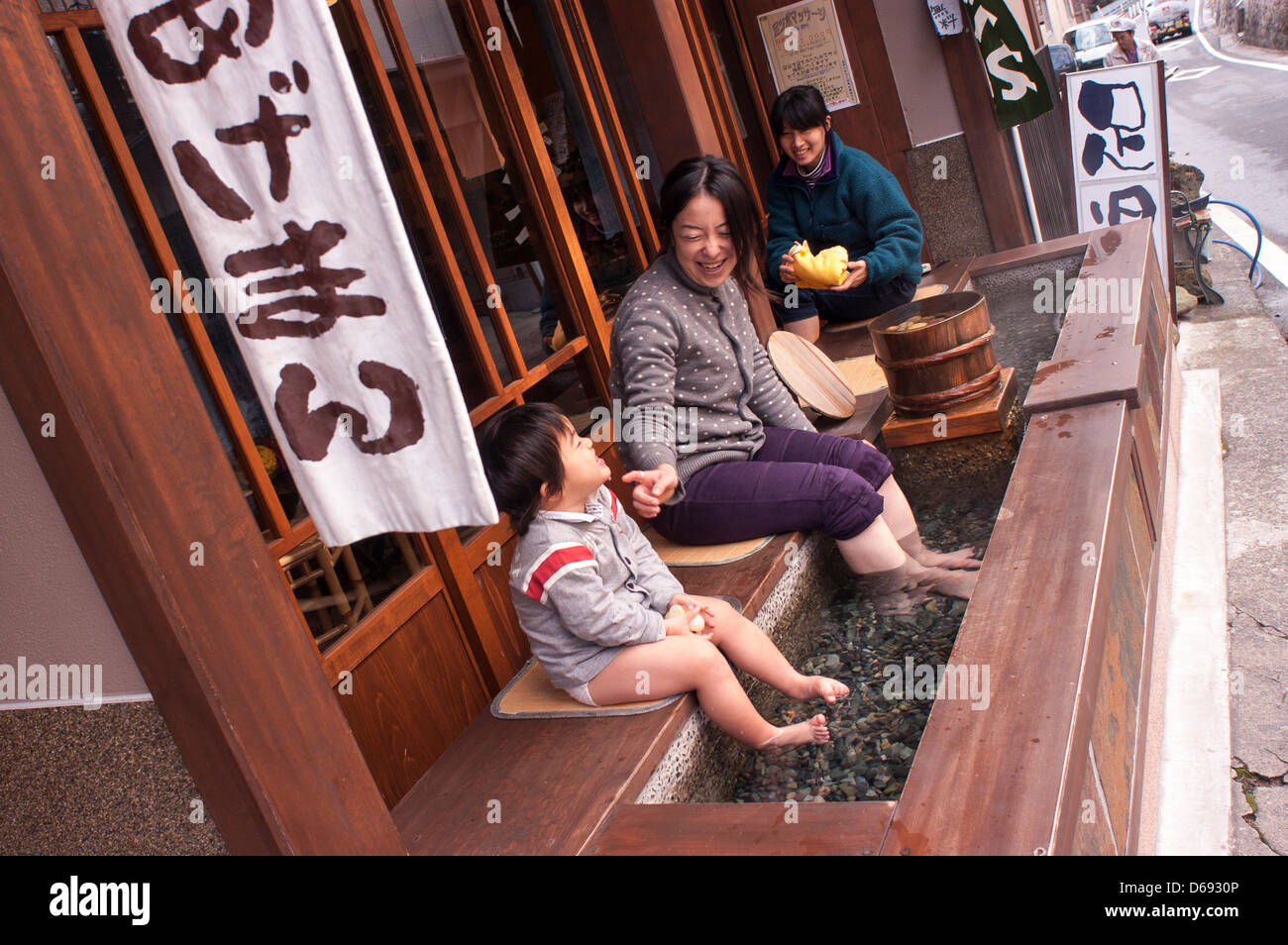 A mother and her son soak their feet in hot spring water outside a shop ...