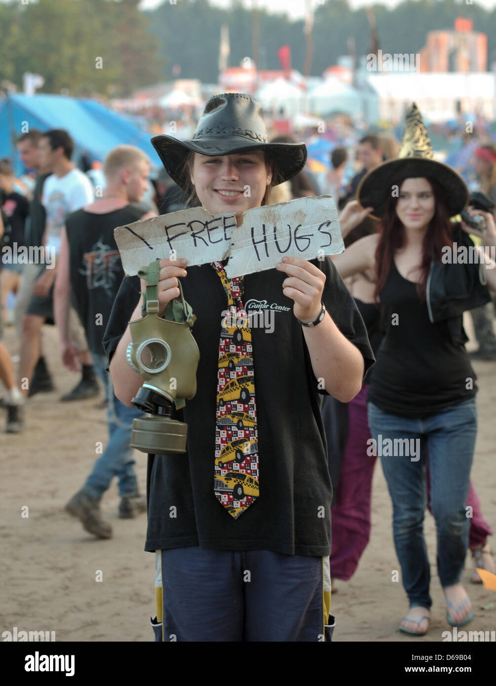 A young man holding a gas mask offerss free hugs at the music festival ...