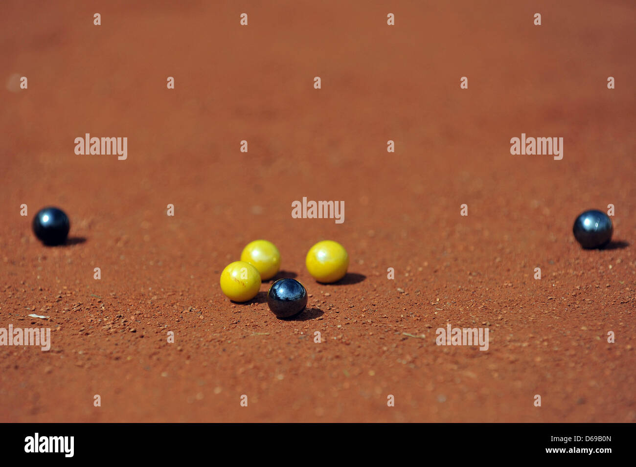 Three yellow and three black marbles lie on a cindered pitch at the ...