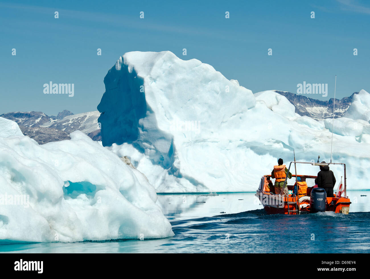 An Inuit steers a boat with tourists between icebergs in the Sermilik ...