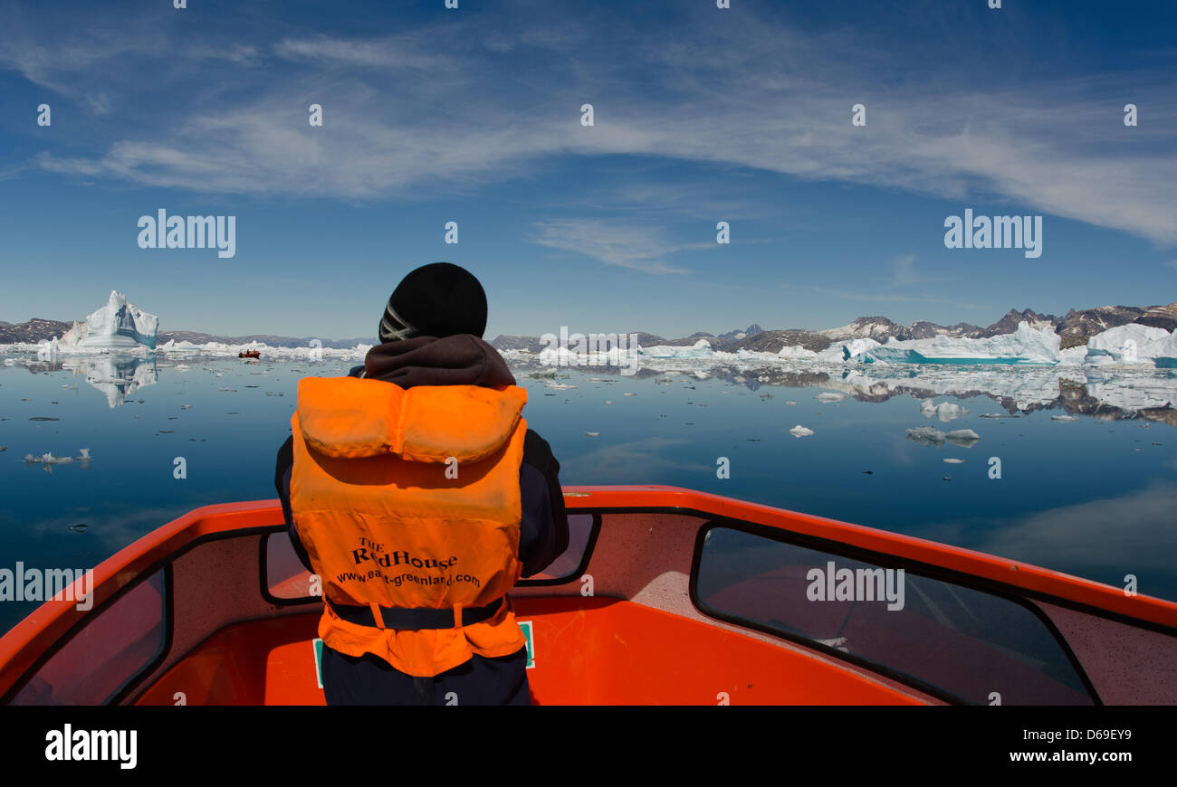 An Inuit steers a boat with tourists between icebergs in the Sermilik ...