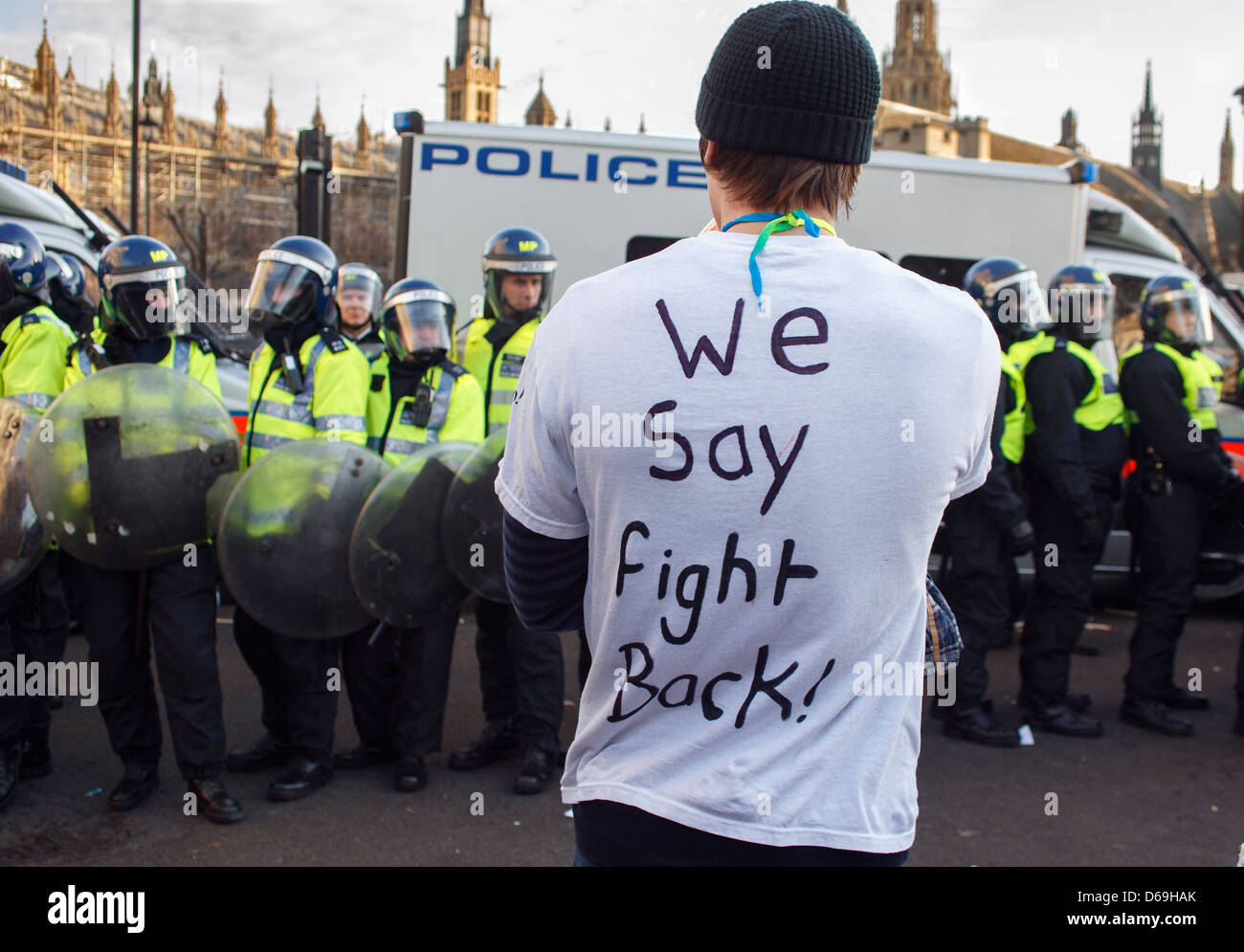 A Student with a slogan on his T-shirt stands in front of riot police ...