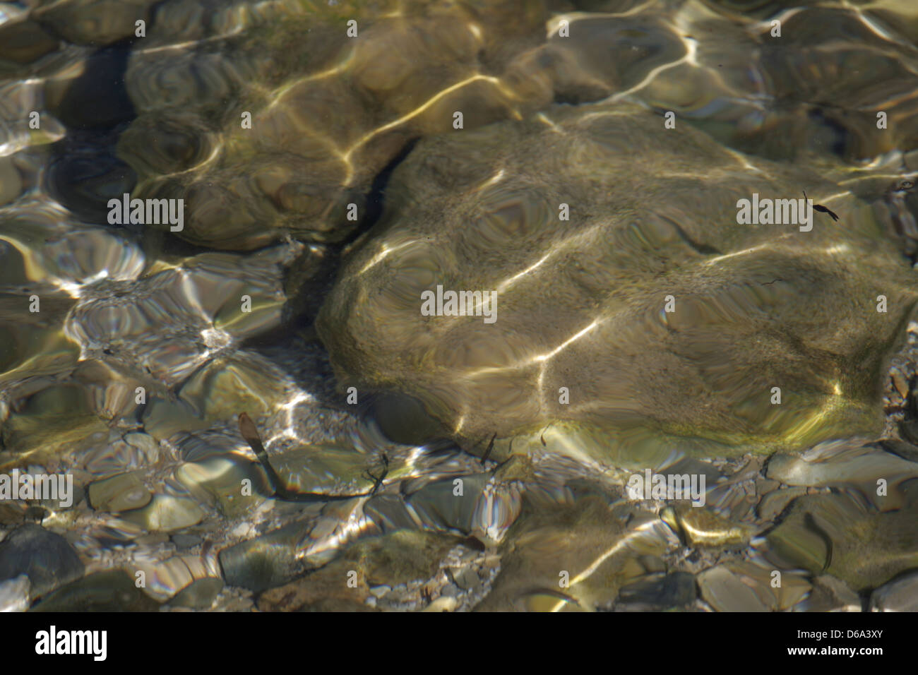 Close up of water playing over pebbles and reflecting sunlight in a ...