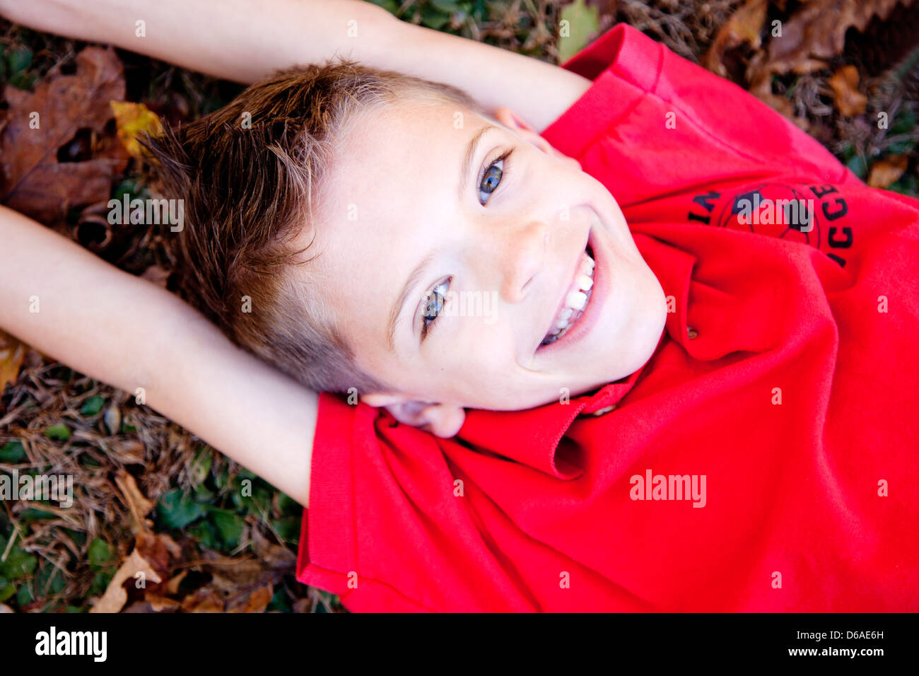 Smiling Boy With Arms Above Head Laying on Ground, High Angle View ...