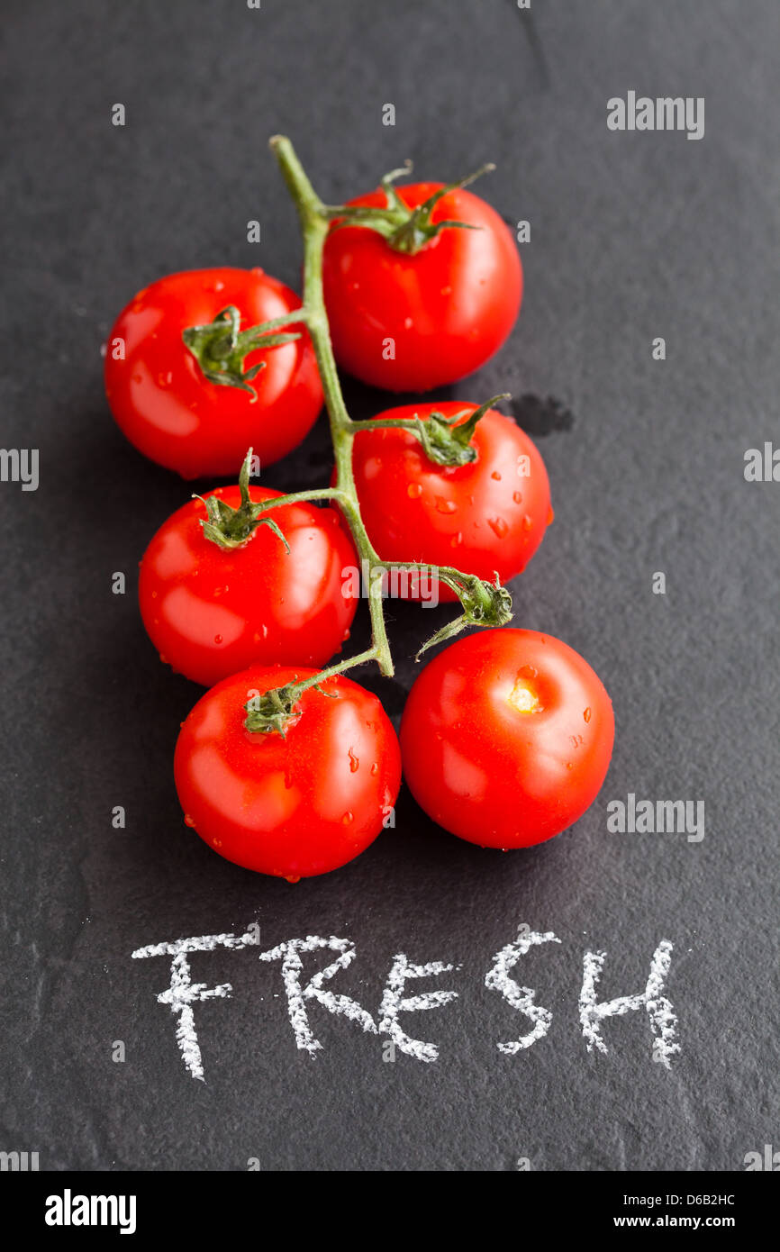 Bunch of fresh red tomatoes with word fresh written in chalk on dark ...