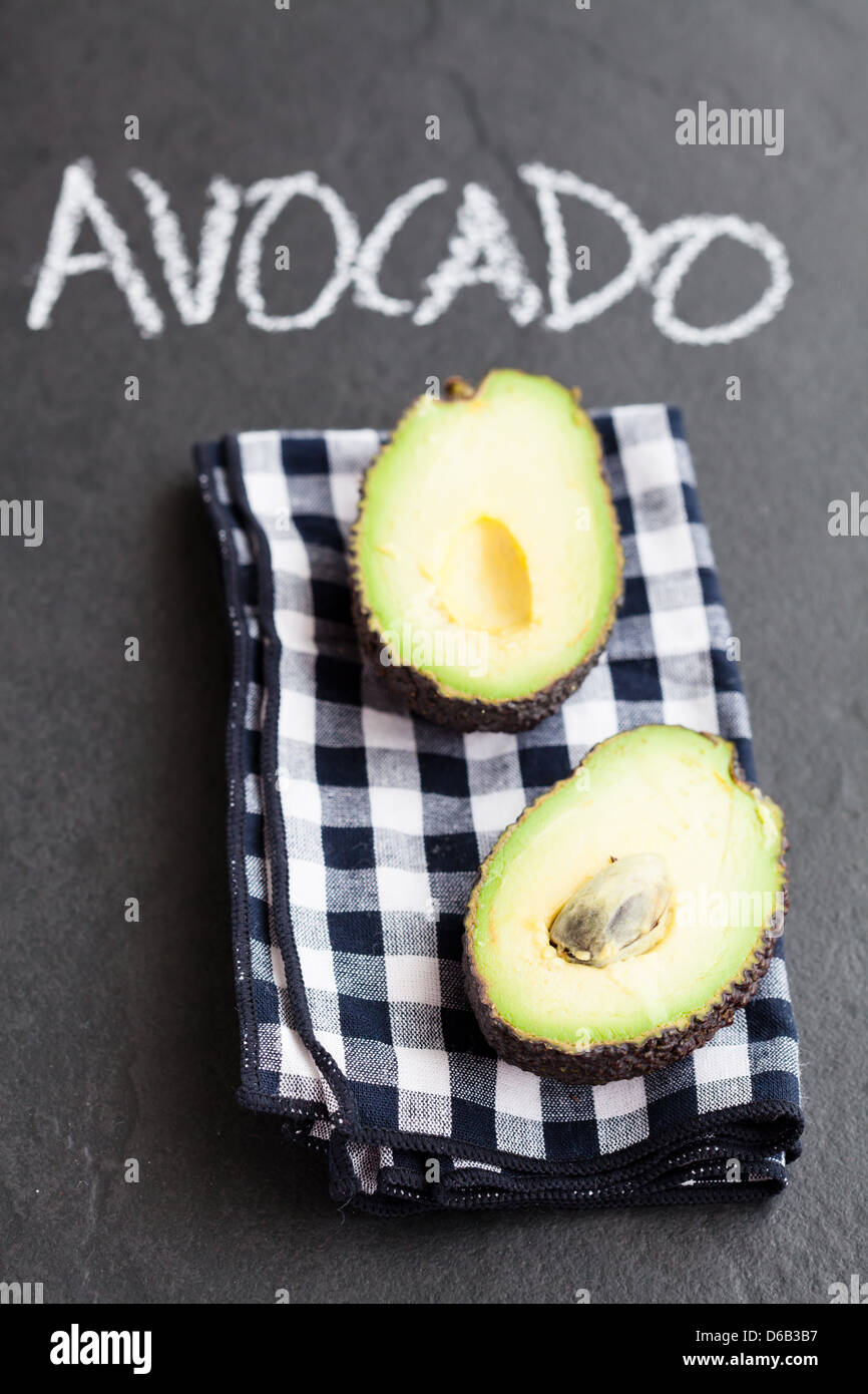 Closeup of fresh avocado halves resting on checkered napkin with word ...