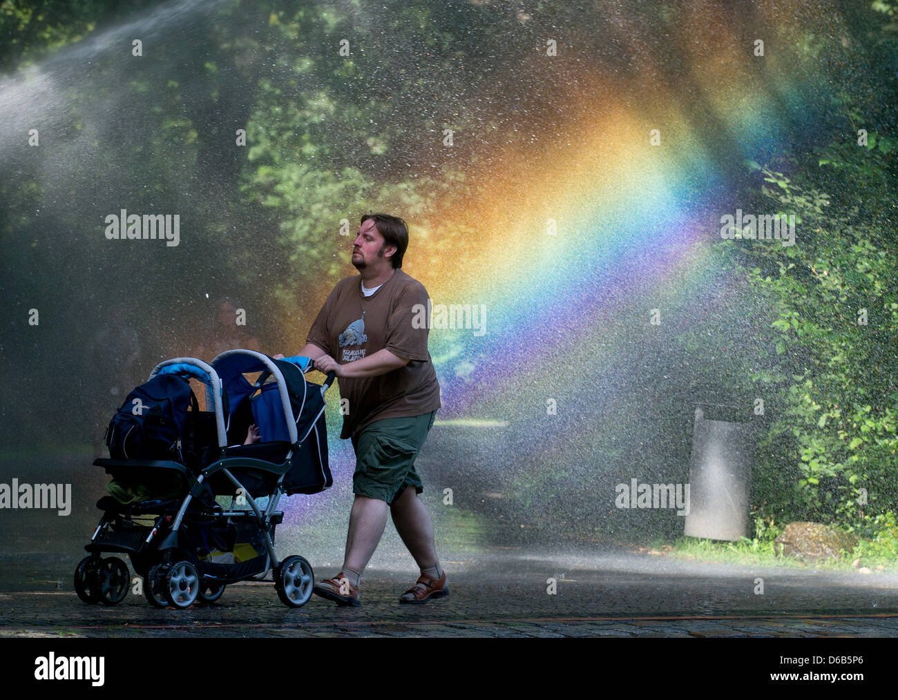A man with baby carriage goes past a rainbow caused by the water of a ...