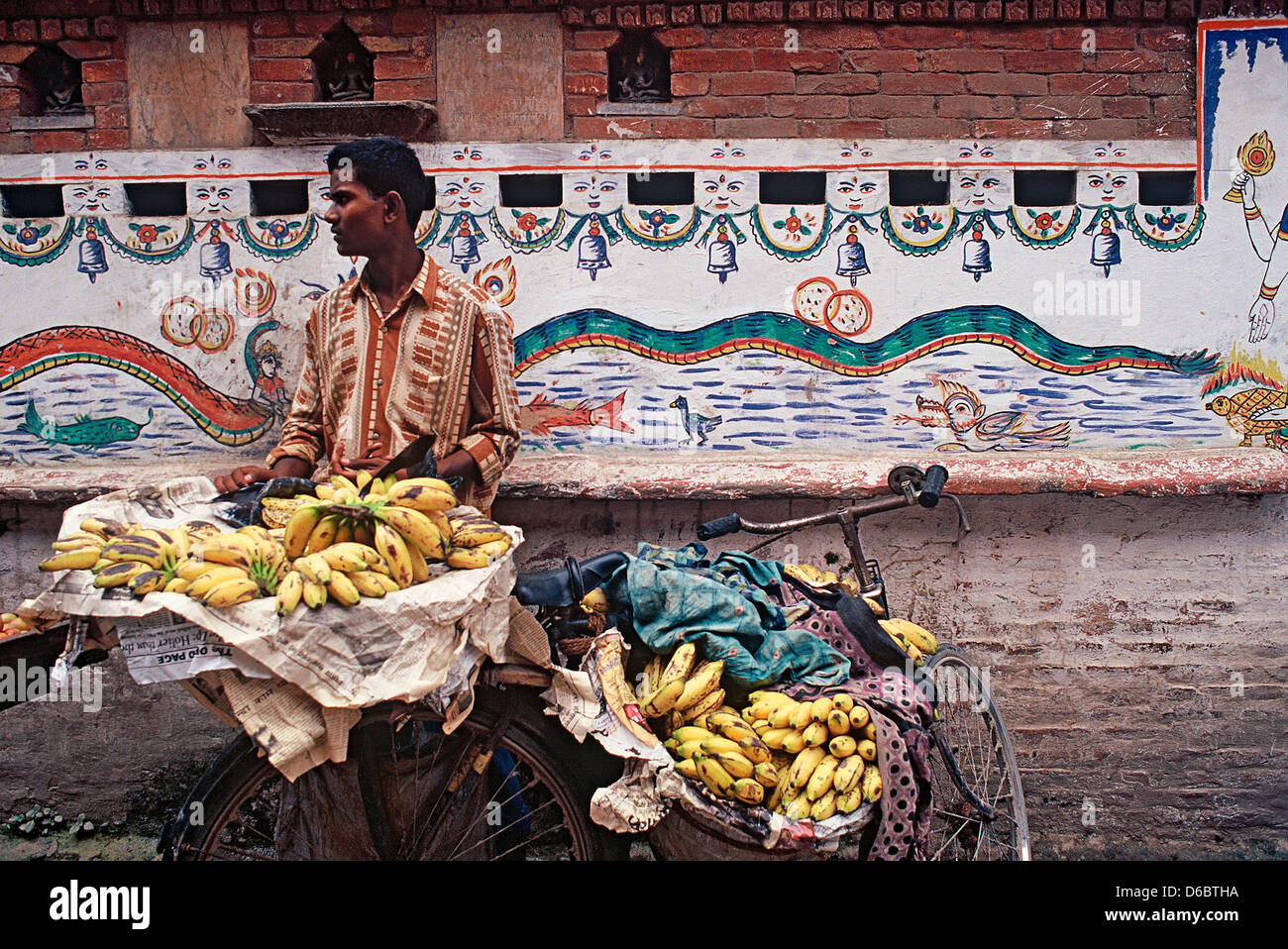 Man selling bananas in a street. Behind him, a mythological hindu ...