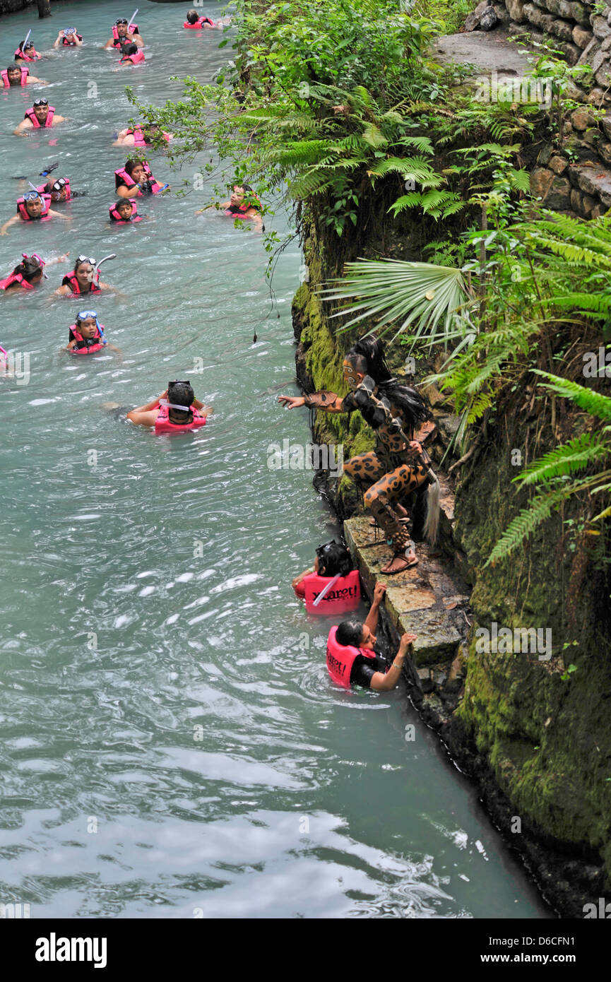 Visitors swimming in a river passing a Mayan village mock-up at Xcaret ...