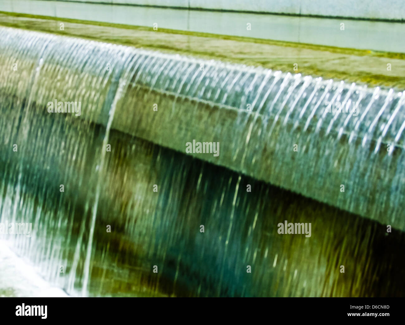 Water flowing over edge of granite wall into a pool of shallow water ...