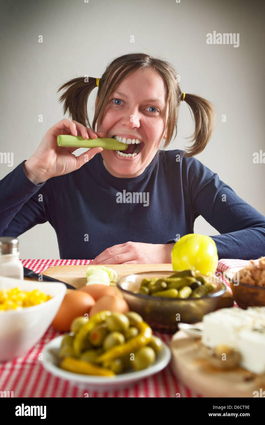 Woman eating leek. Beautiful smiling woman with pigtails bites leek ...
