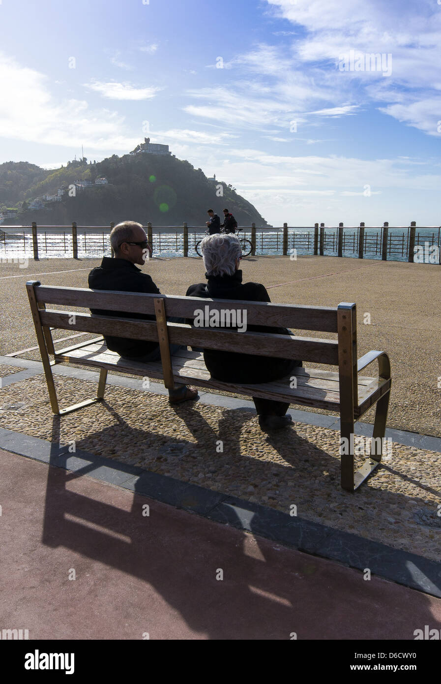 Couple sitting on the seafront bench with Monte Igueldo in the distance ...