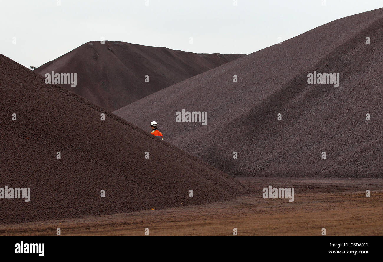 An employee walks past various piles of iron ore pellets on a storage ...