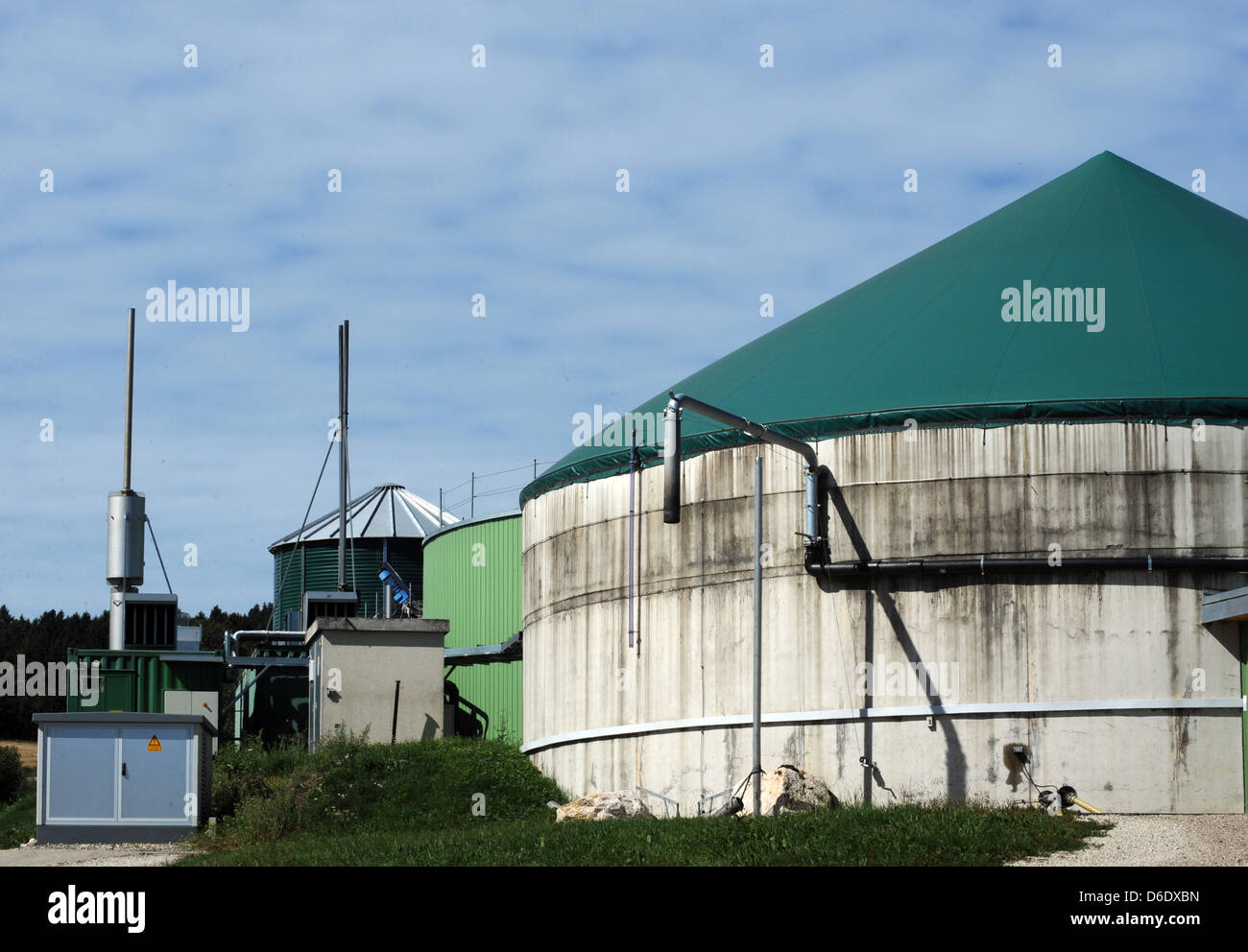 A small biogas plant rises above the green gras of a farming meadow in ...