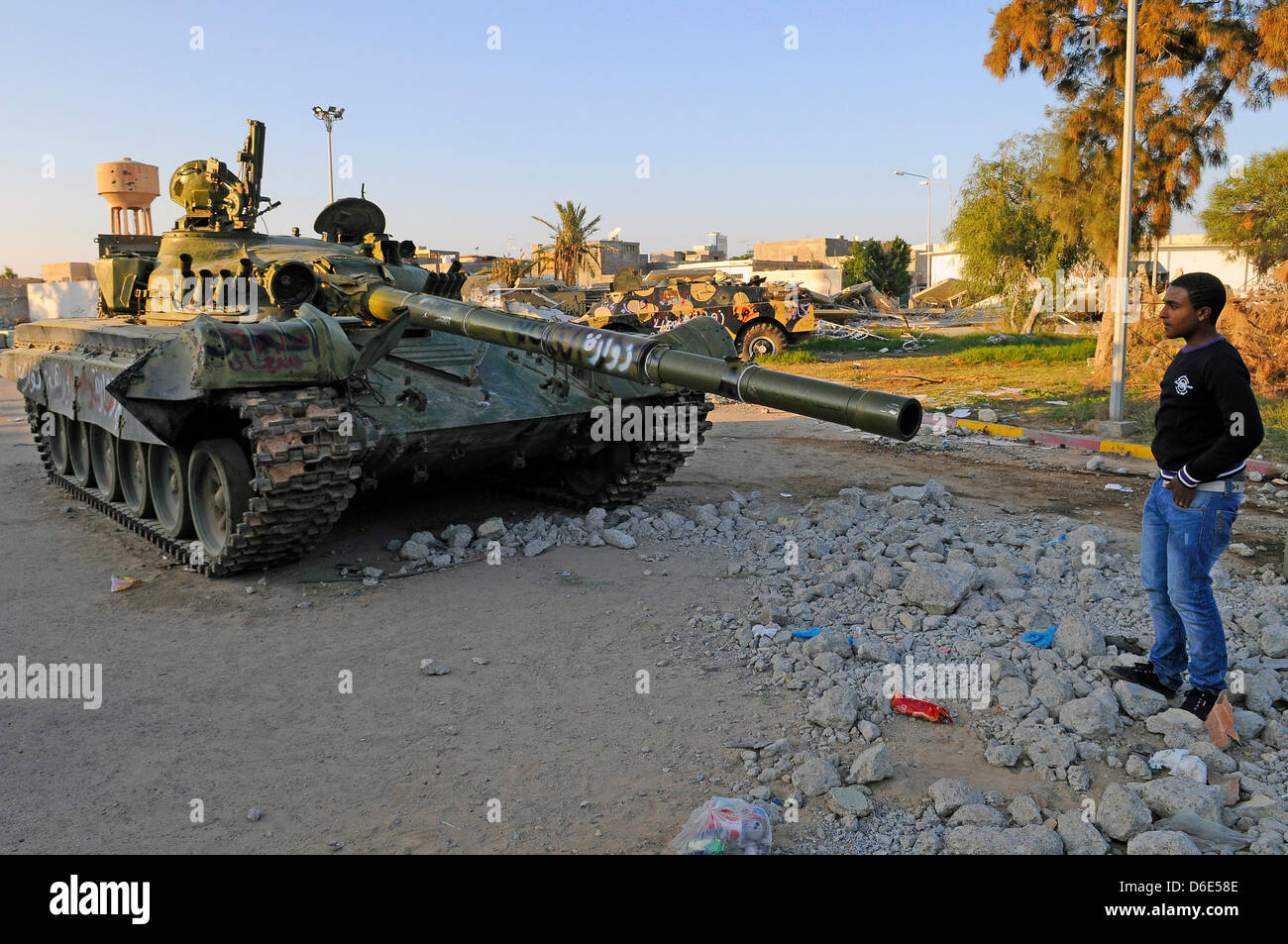 A young man stands in front of a deserted tank in the Bab al-Azizia ...