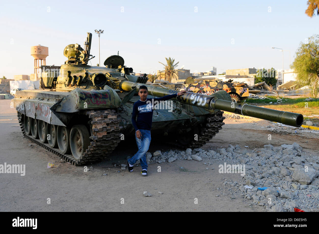 A young man stands in front of a deserted tank in the Bab al-Azizia ...