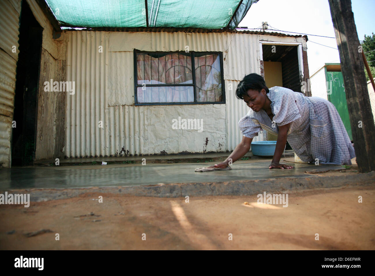 An African woman washes the porch of her tin shack home on her h Stock ...