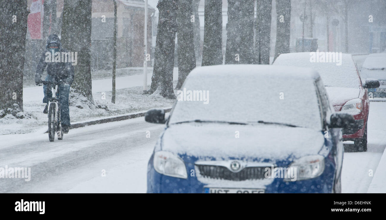 Parked cars are covered with snow and a man cycles down a treet while ...