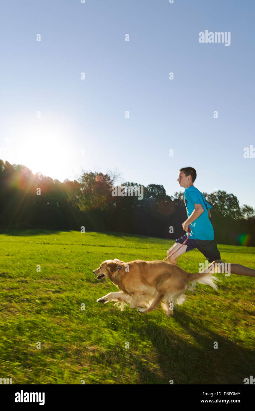 Teenage boy running with his Golden Retriever dog in the green grassy ...