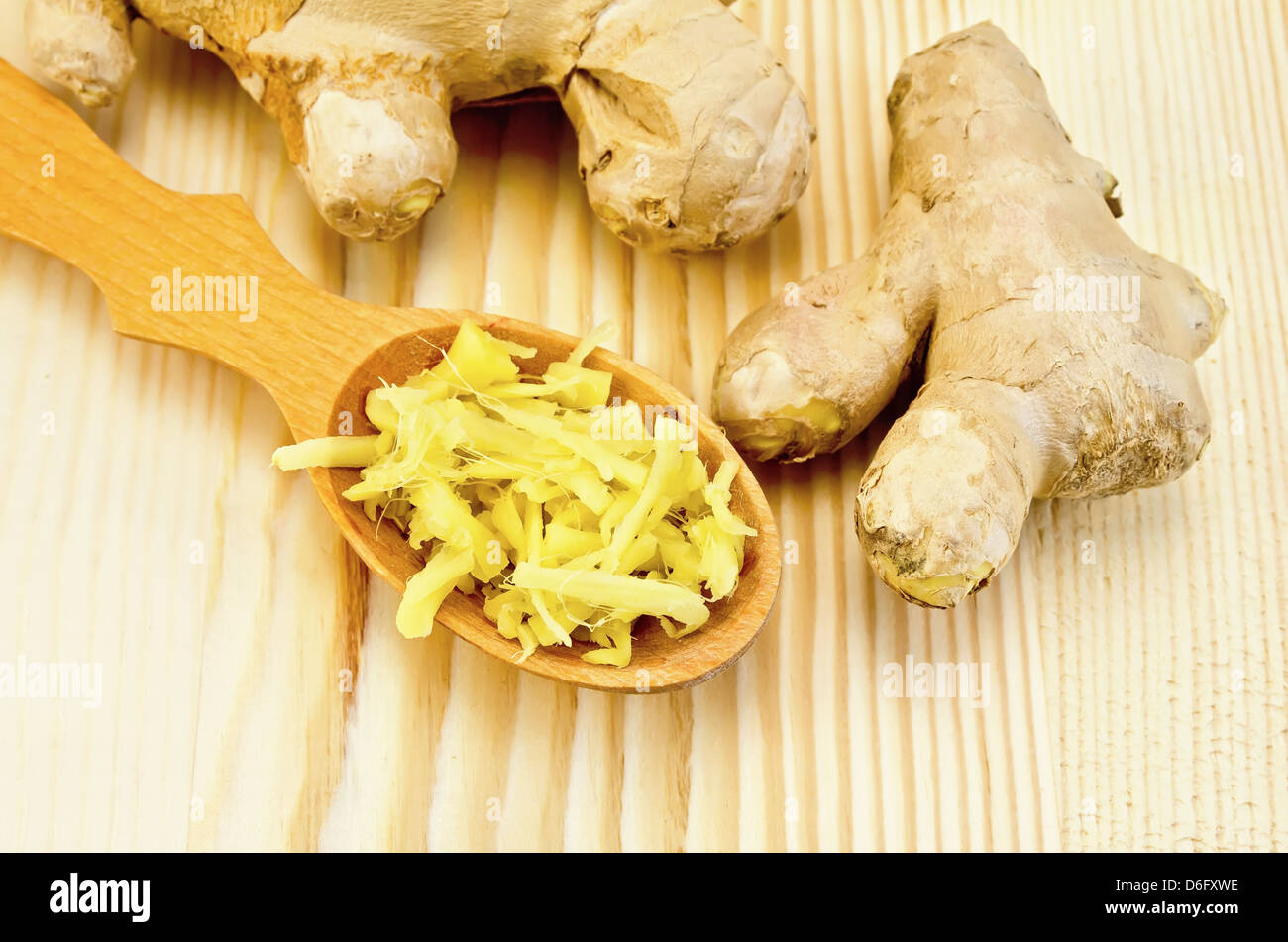 Wooden spoon with grated ginger, ginger root against a wooden board ...