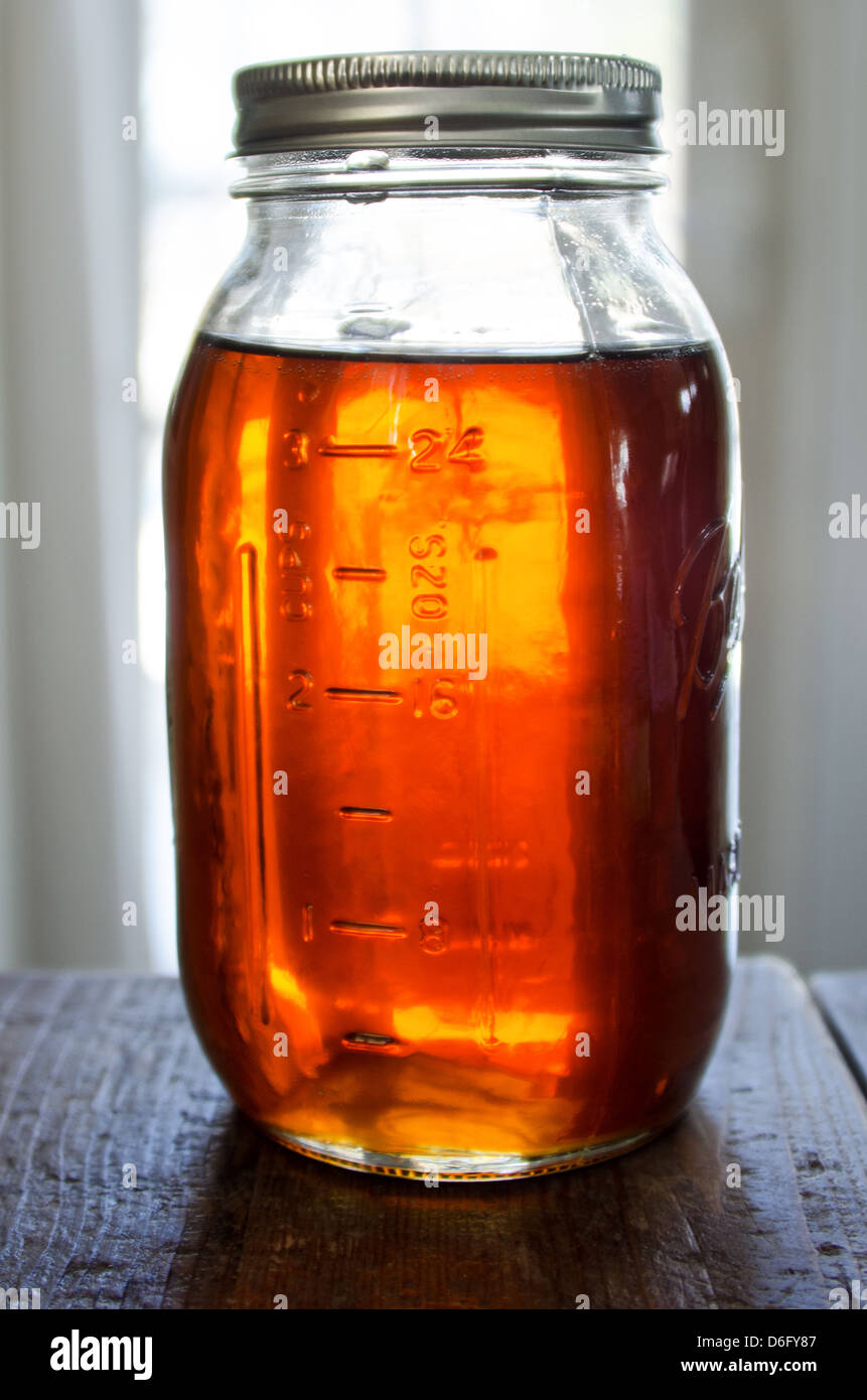 A glass mason jar full of Maine maple syrup stands on a rustic wood ...