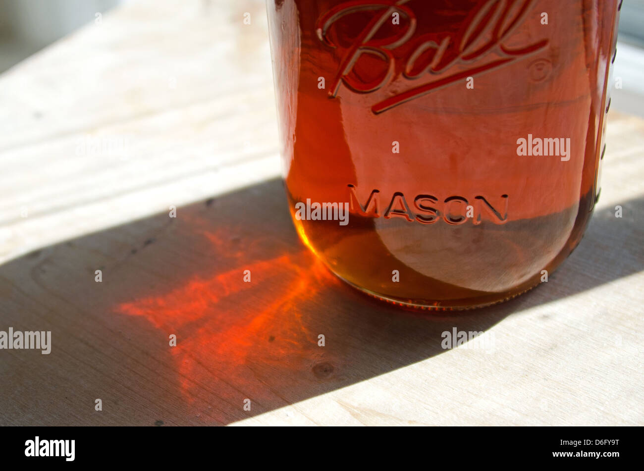 Sunlight casts amber patterns as it filters through a glass mason jar ...