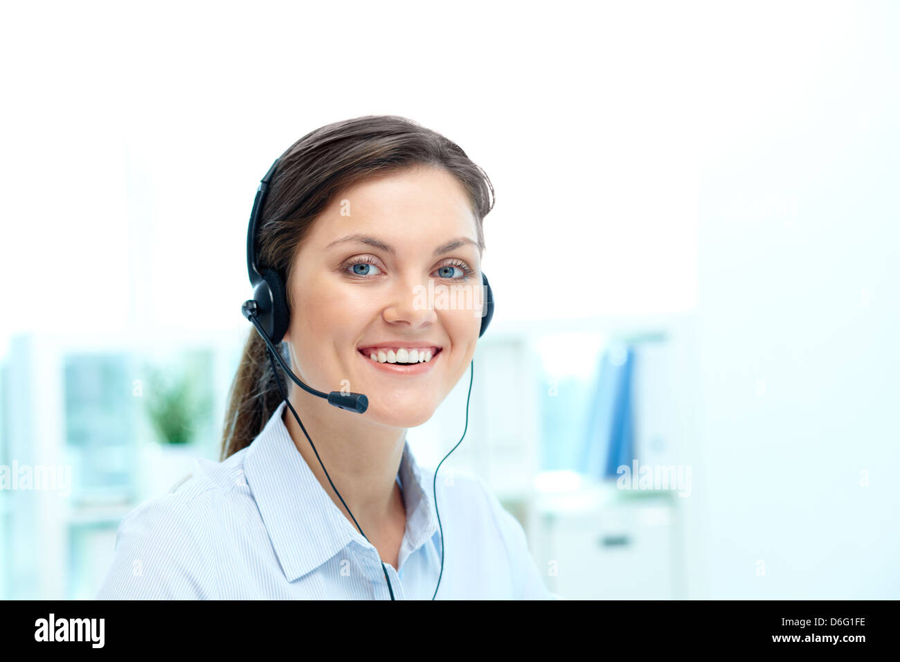 Portrait of young operator with headset looking at camera with friendly ...