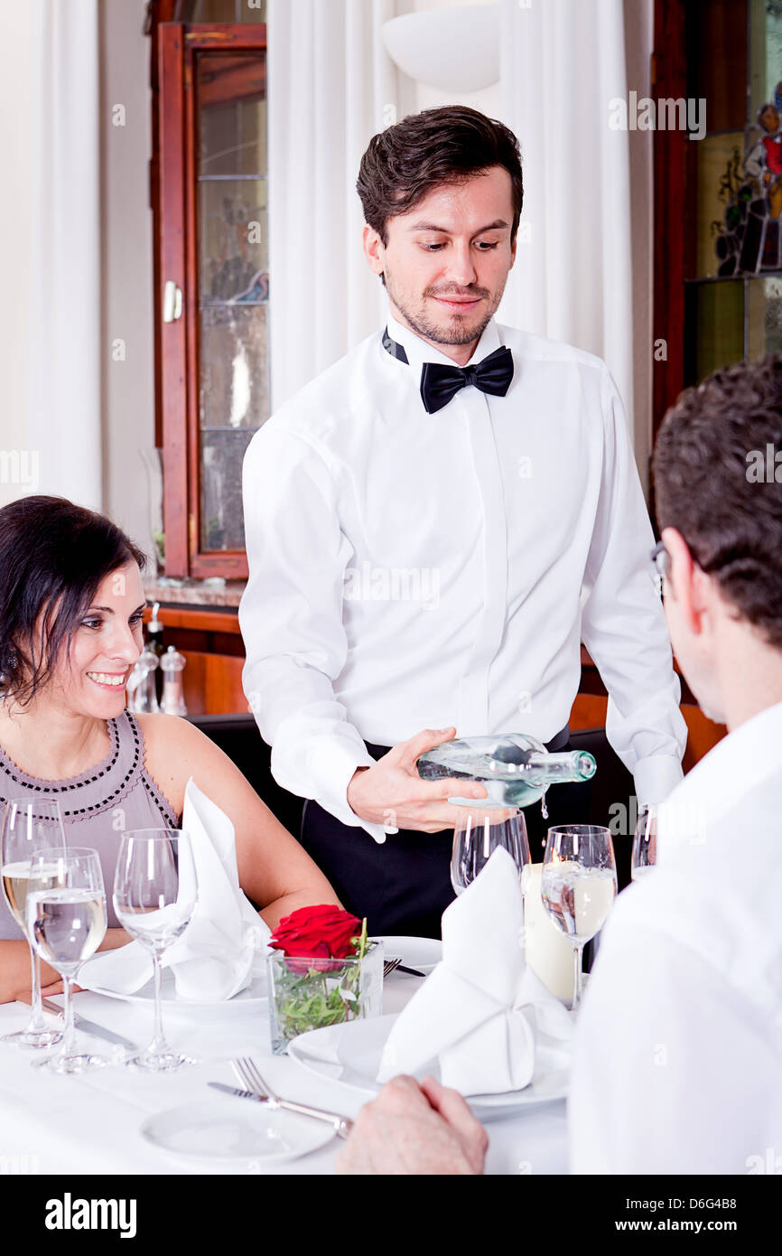 man and woman for dinner in restaurant waiter serving mineral water ...
