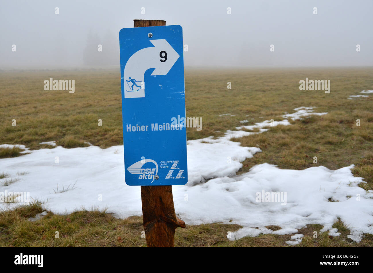 A cross country skiing sign stands in a field with the remnants of snow ...