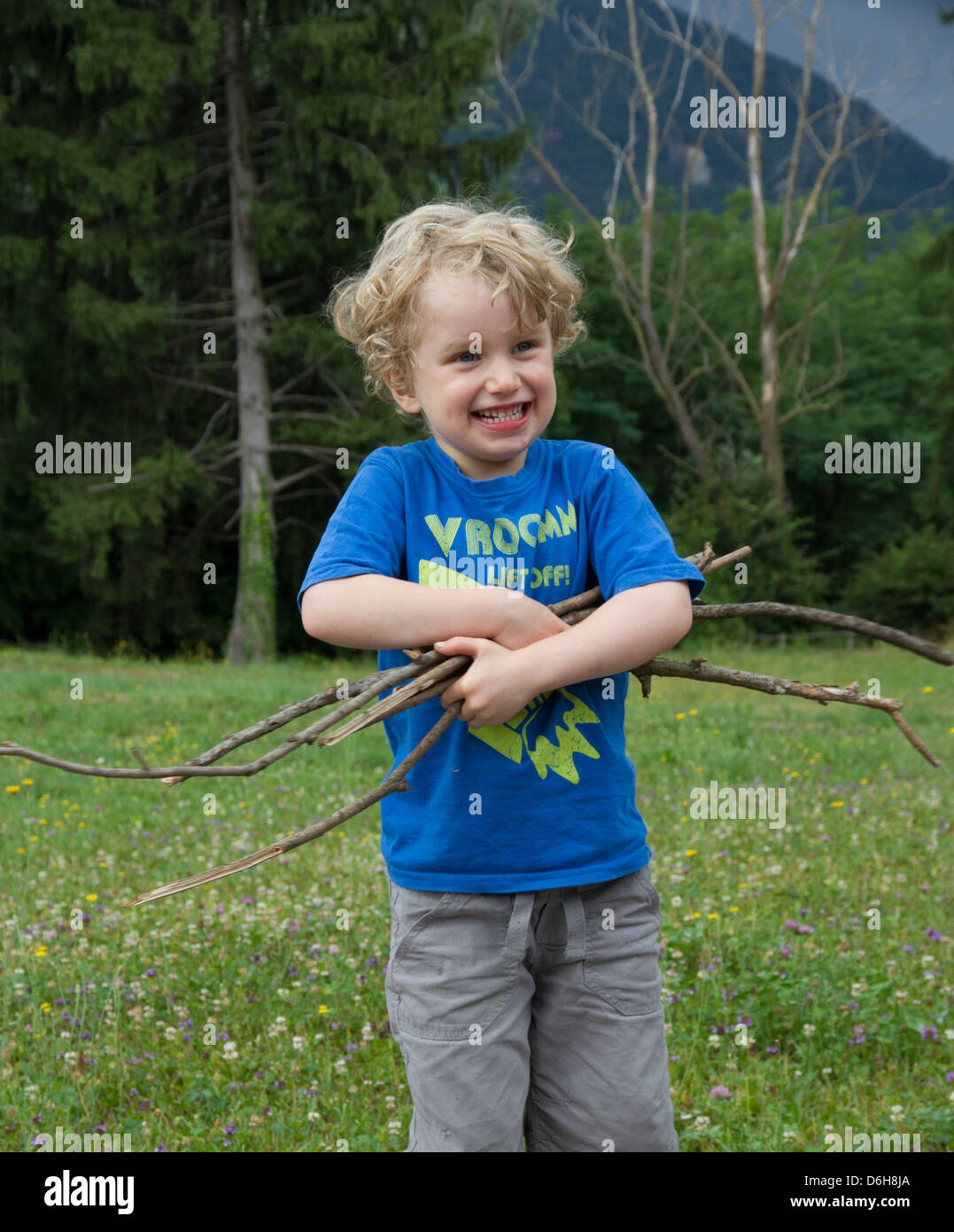 Young boy outdoors collecting sticks by the woods and smiling Stock ...