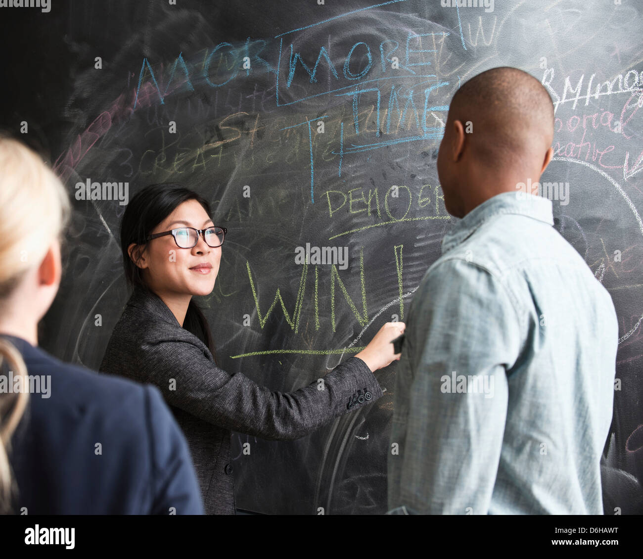 Woman writing on blackboard, colleagues watching Stock Photo - Alamy