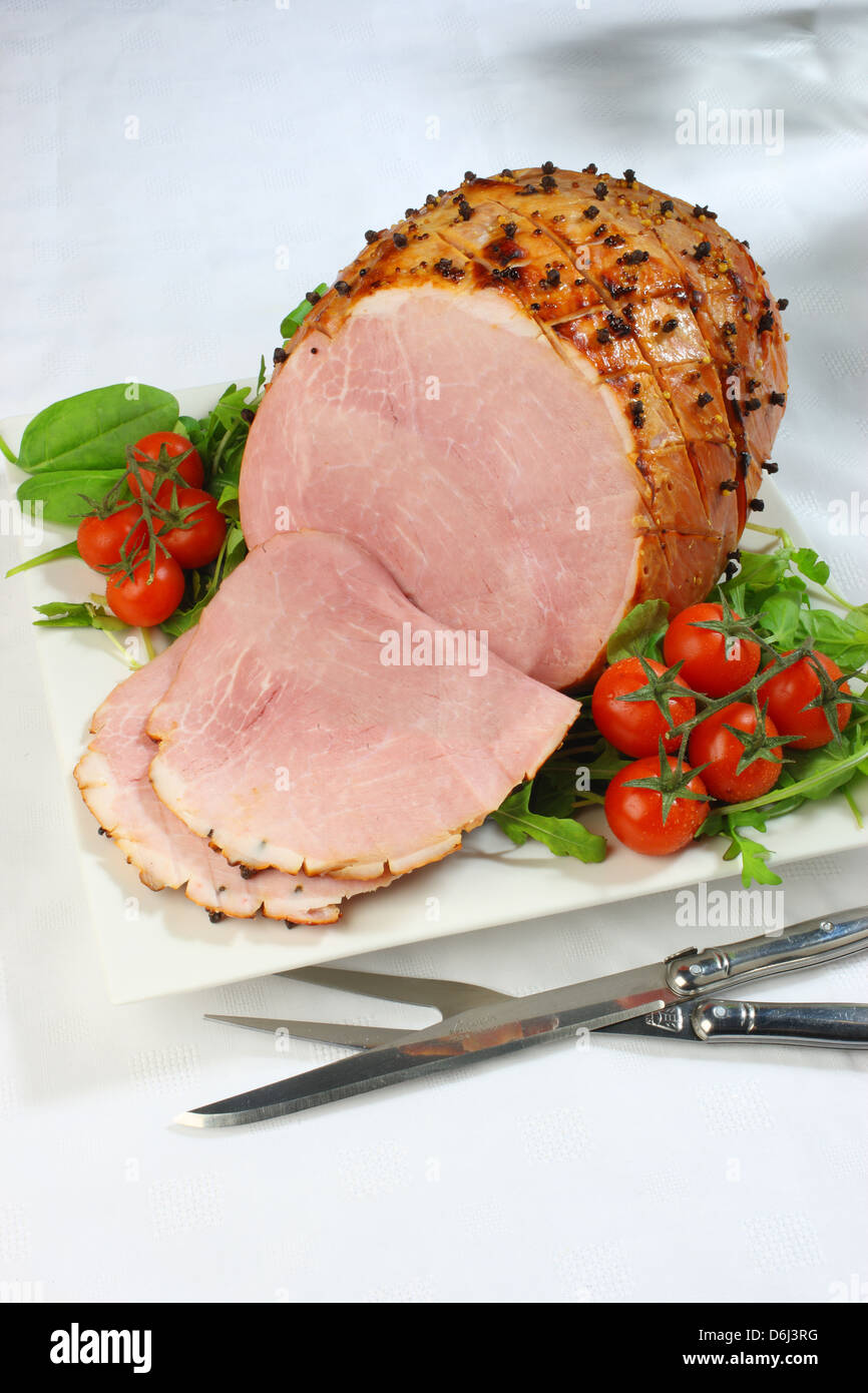 Baked Ham with cloves and cherry tomatoes and carving knife and fork on ...