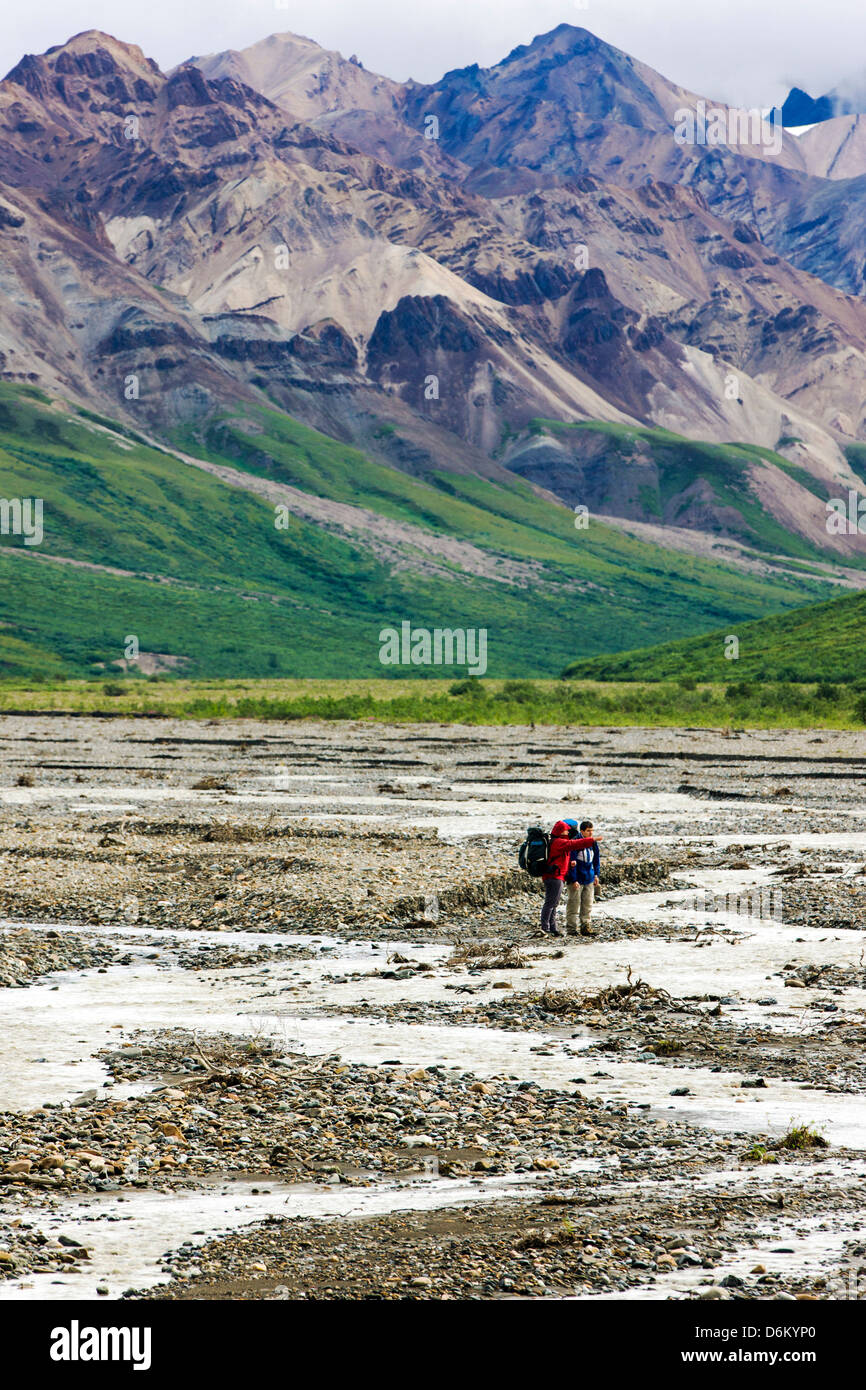 Two backpackers carefully fiord the Toklat River, Denali National Park ...