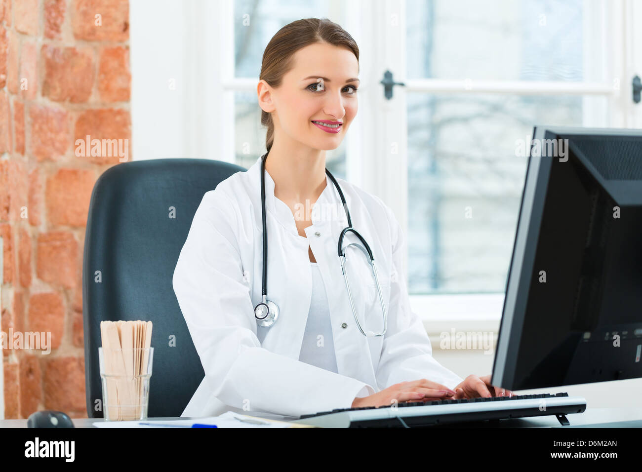 Young female doctor sitting at a desk in front of window in clinic ...