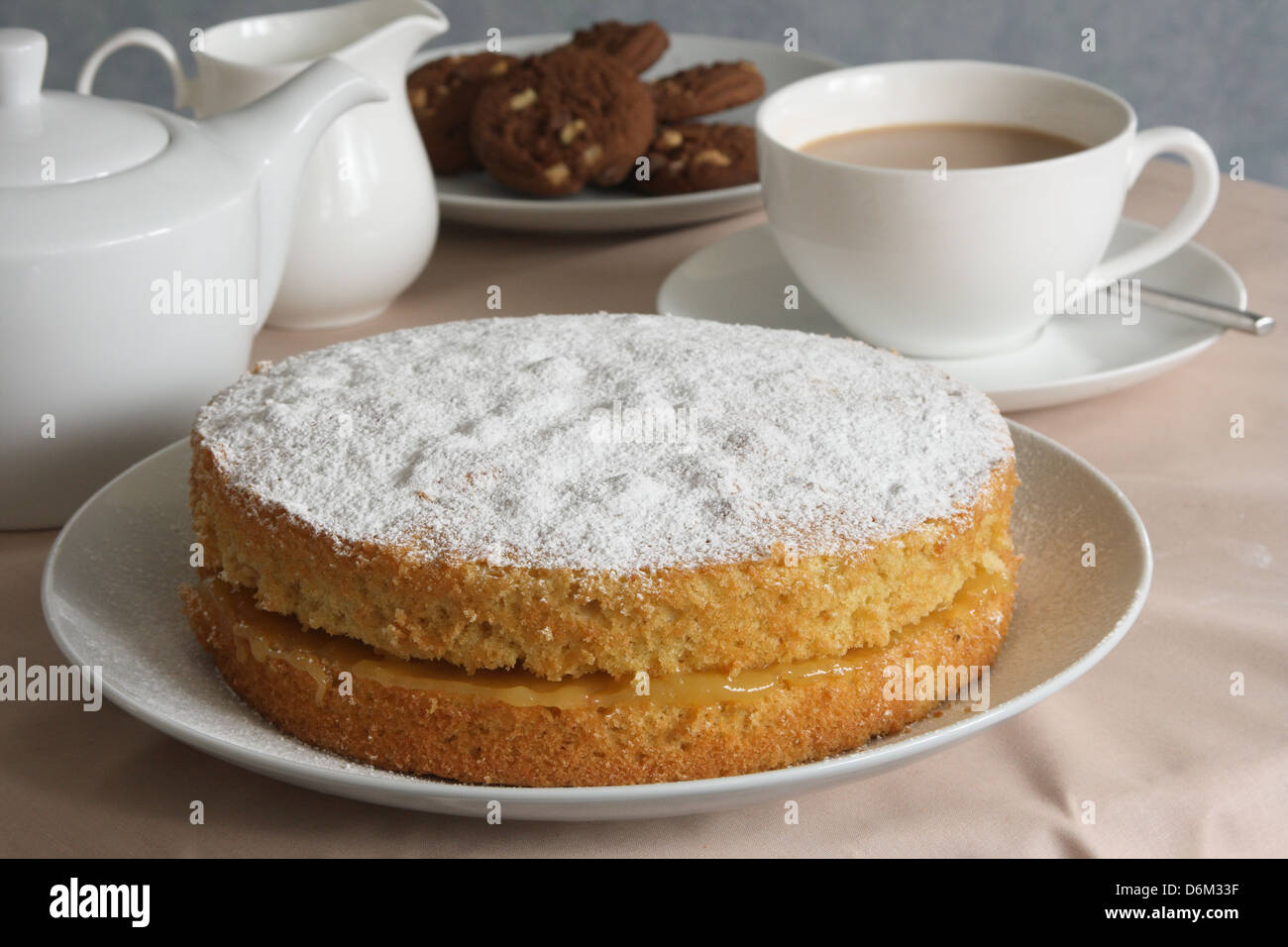 A lemon victoria sponge cake served with a cup of tea and biscuits ...
