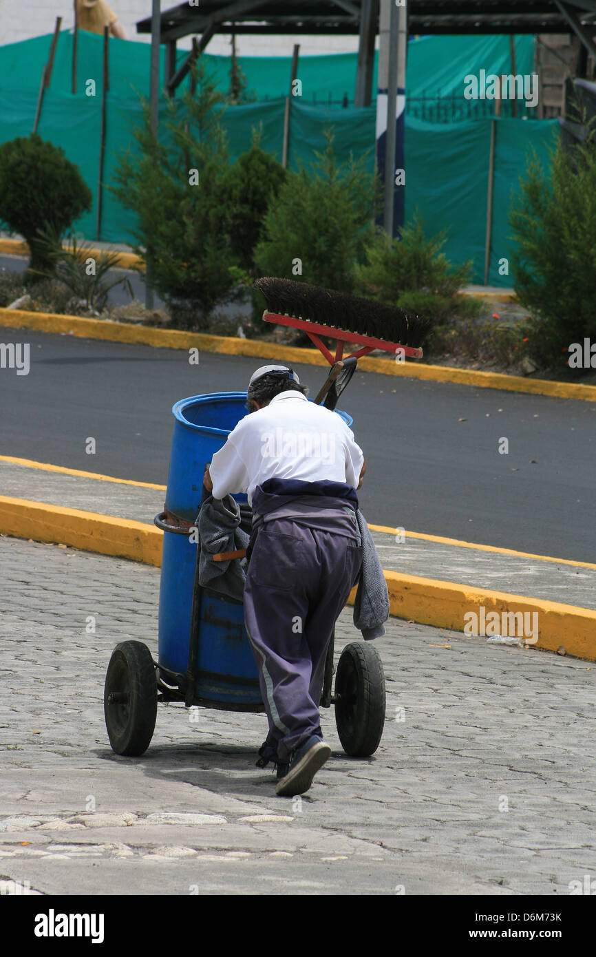 A man pushing a large portable garbage bin down a street in Cotacachi ...