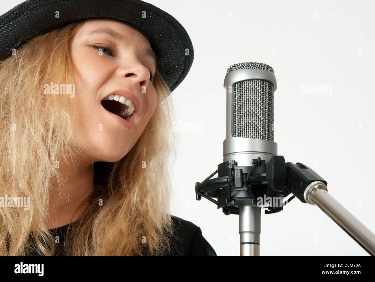 Young woman in black hat singing with studio microphone. Isolated on ...