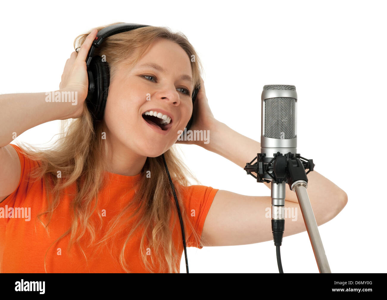 Young woman in orange t-shirt singing with studio microphone. Isolated ...