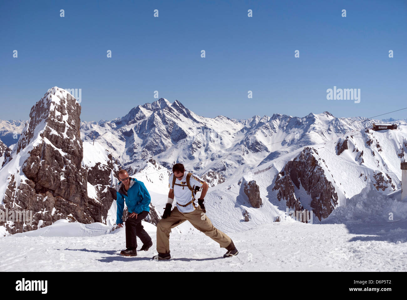 Two men performing pre-skiing warm-up stretching exercises, at altitude ...