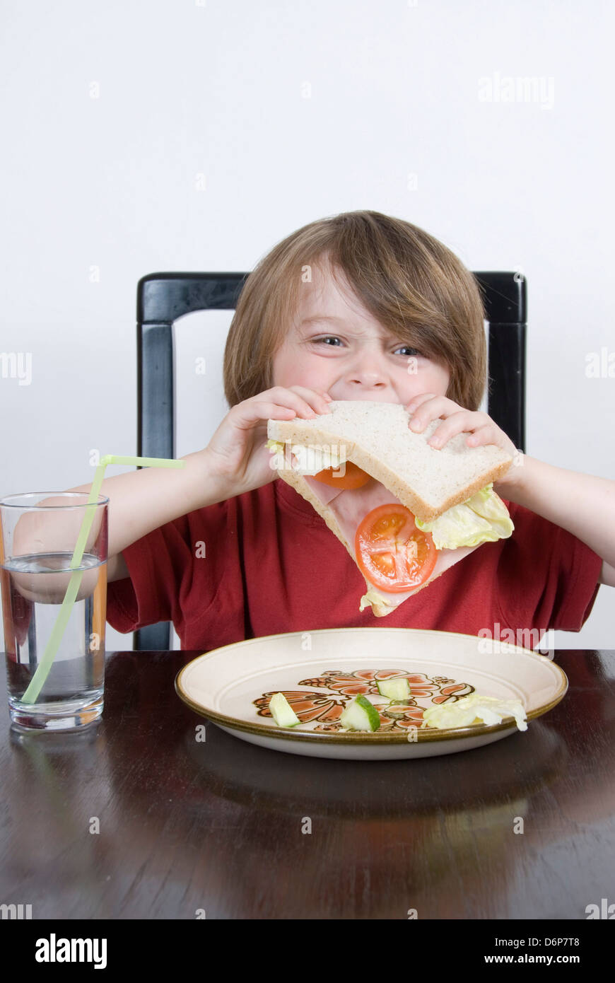 Boy eating a large ham sandwich with salad falling back to his plate ...