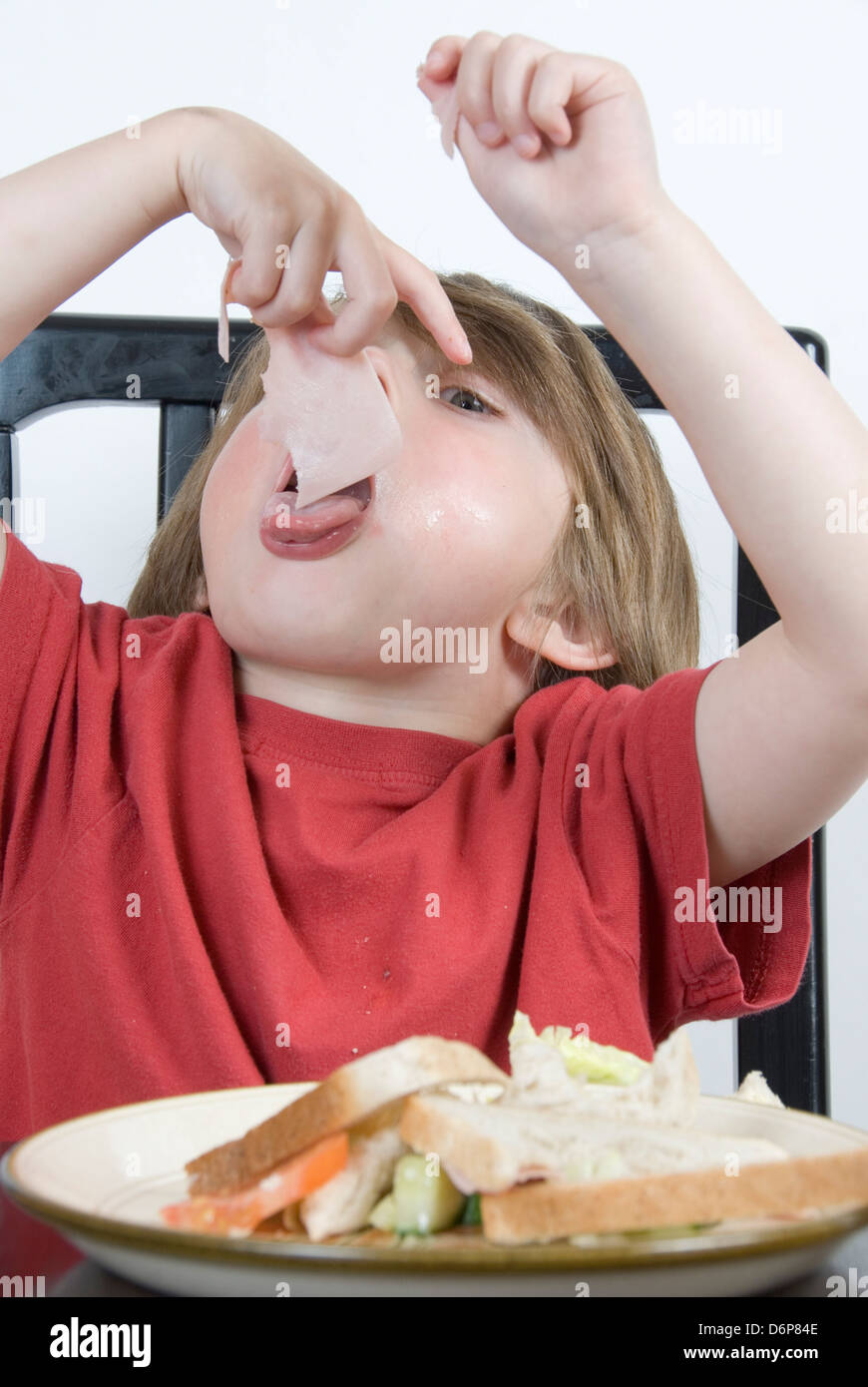 Young boy eating a slice of ham picked out from the middle of his salad ...