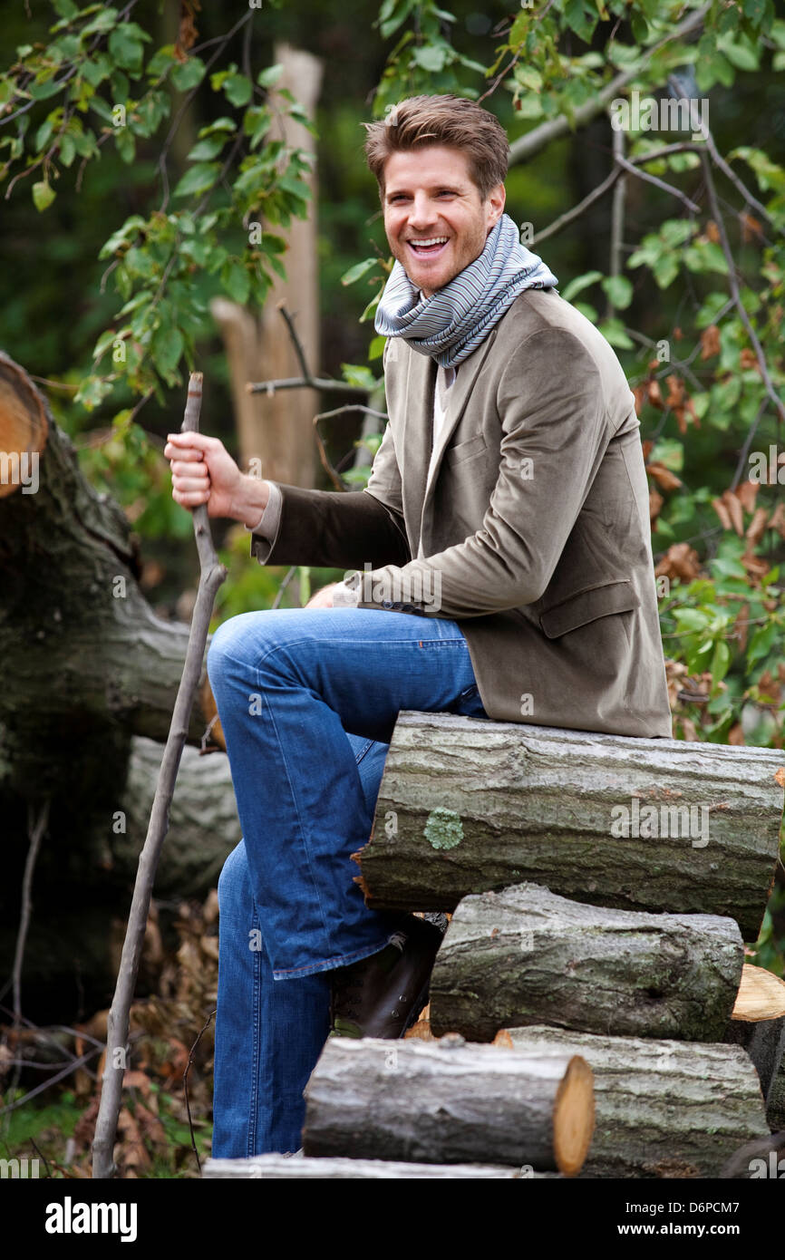 Young man sitting on log in forest Stock Photo - Alamy
