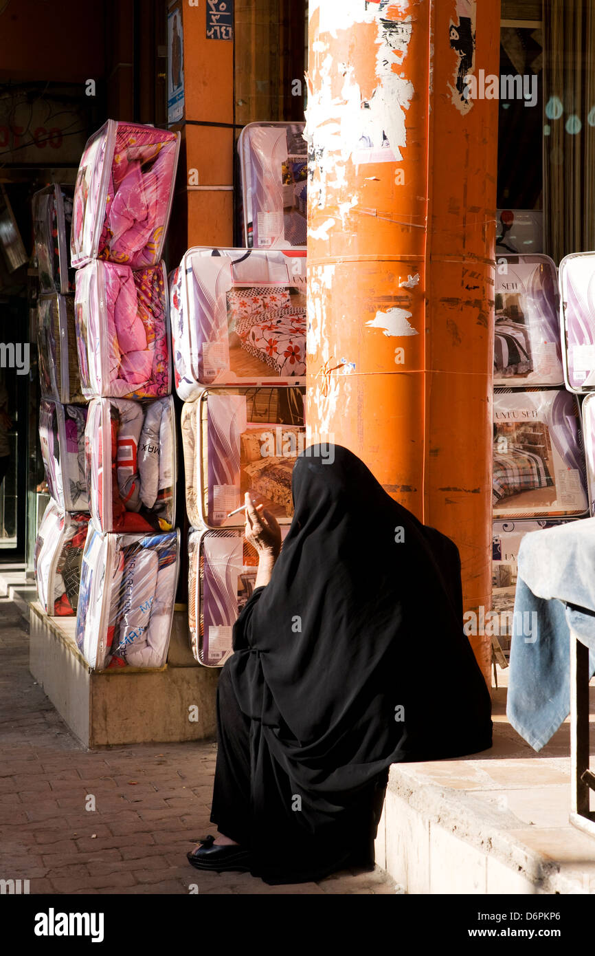 An Iraqi woman in traditional burka sitting and smoking on the street ...