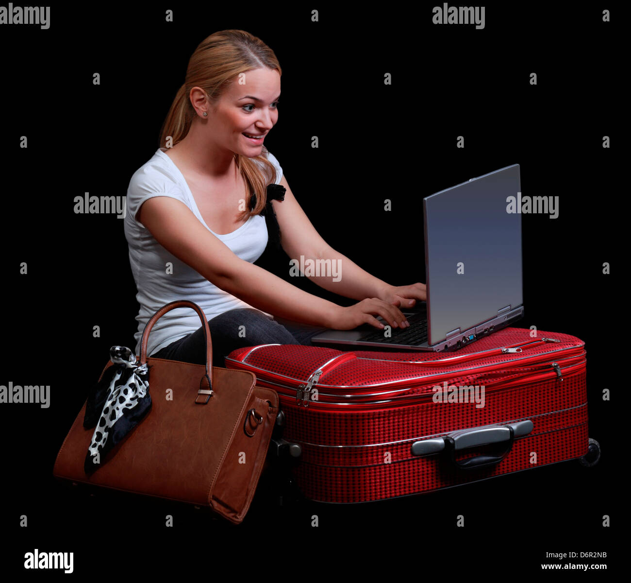 Young blonde woman checking her computer in a hurry on her red suitcase ...
