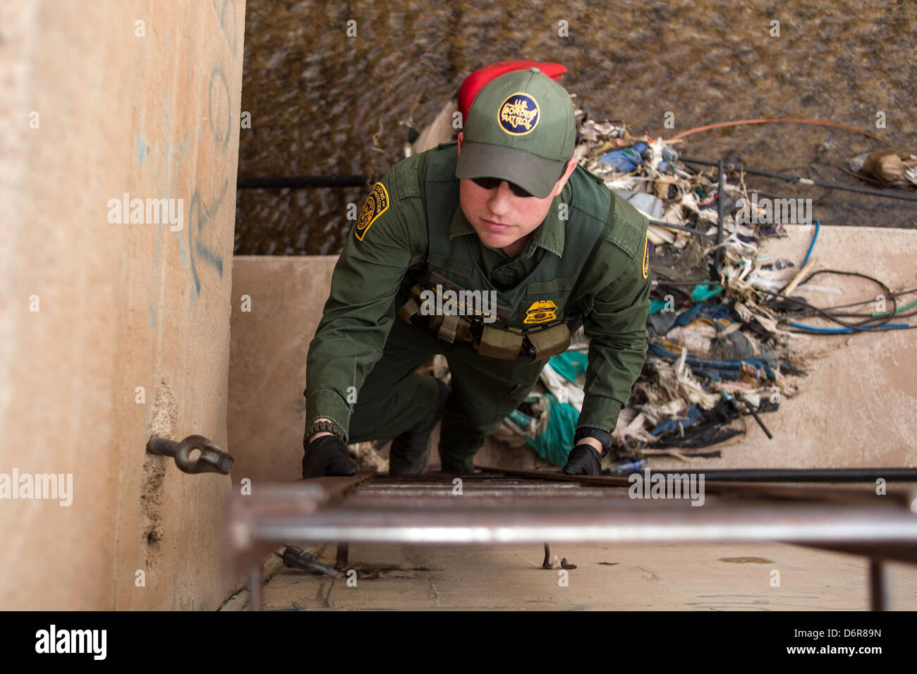 US Customs and Border patrol officer climbs a ladder to a roof along ...
