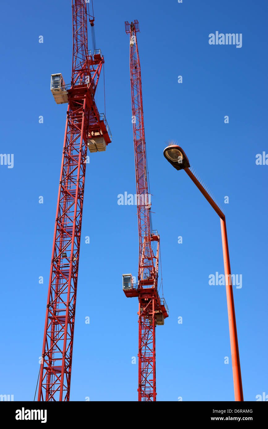 Two red cranes and a red lamp post towering high up above a building ...