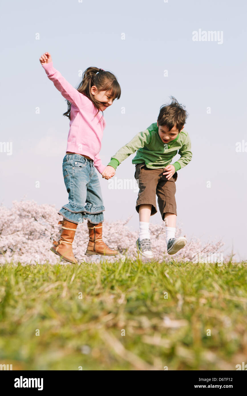 Children holding hands jumping on grassland Stock Photo - Alamy